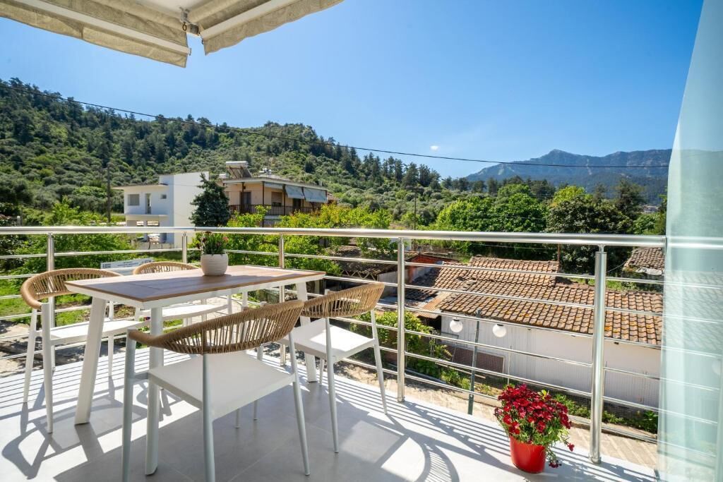 Varanda com mesa, cadeiras, planta em vaso e vista para um morro com edifícios.