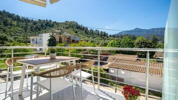 Varanda com mesa, cadeiras, planta em vaso e vista para um morro com edifícios.