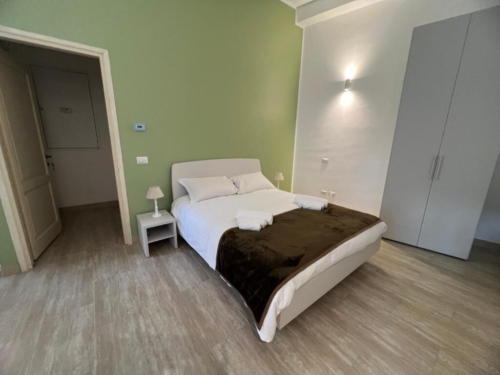 Quarto com cama, mesa de cabeceira, abajur, guarda-roupa e uma porta.