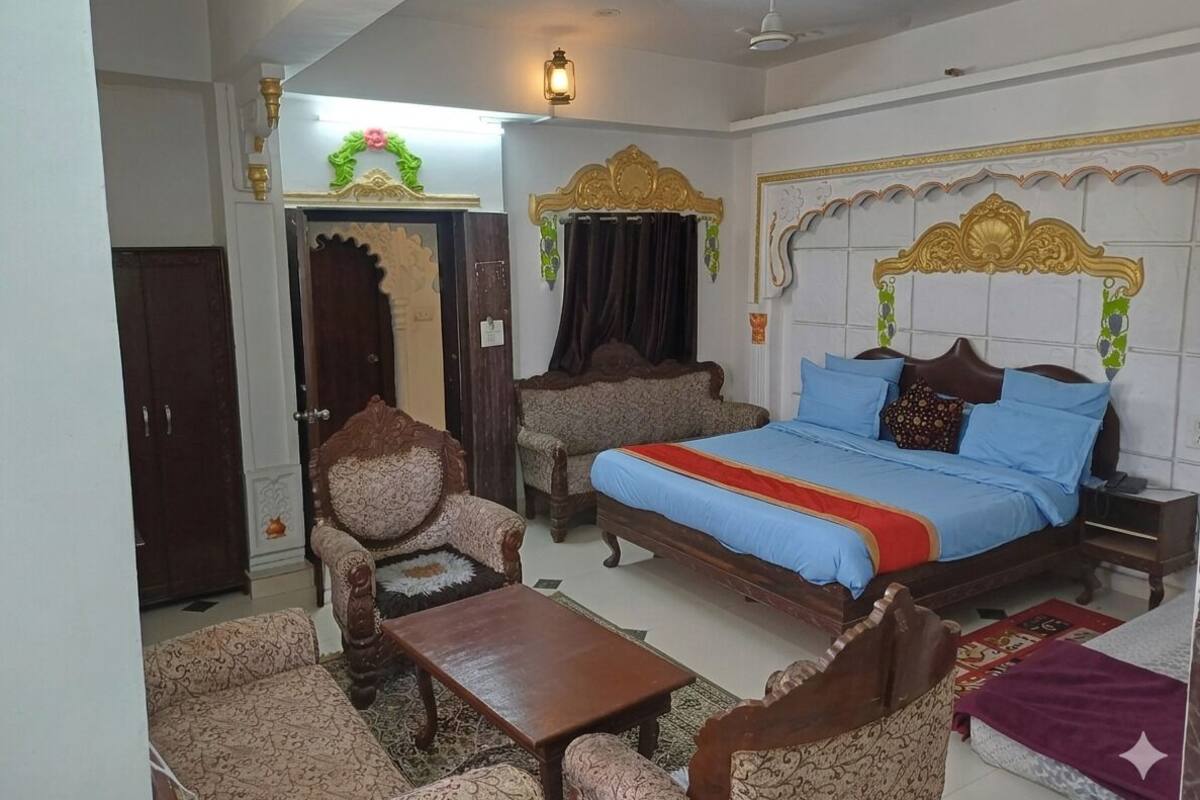 Quarto com cama, duas cadeiras, uma mesa, guarda-roupa e ventoinha no teto.