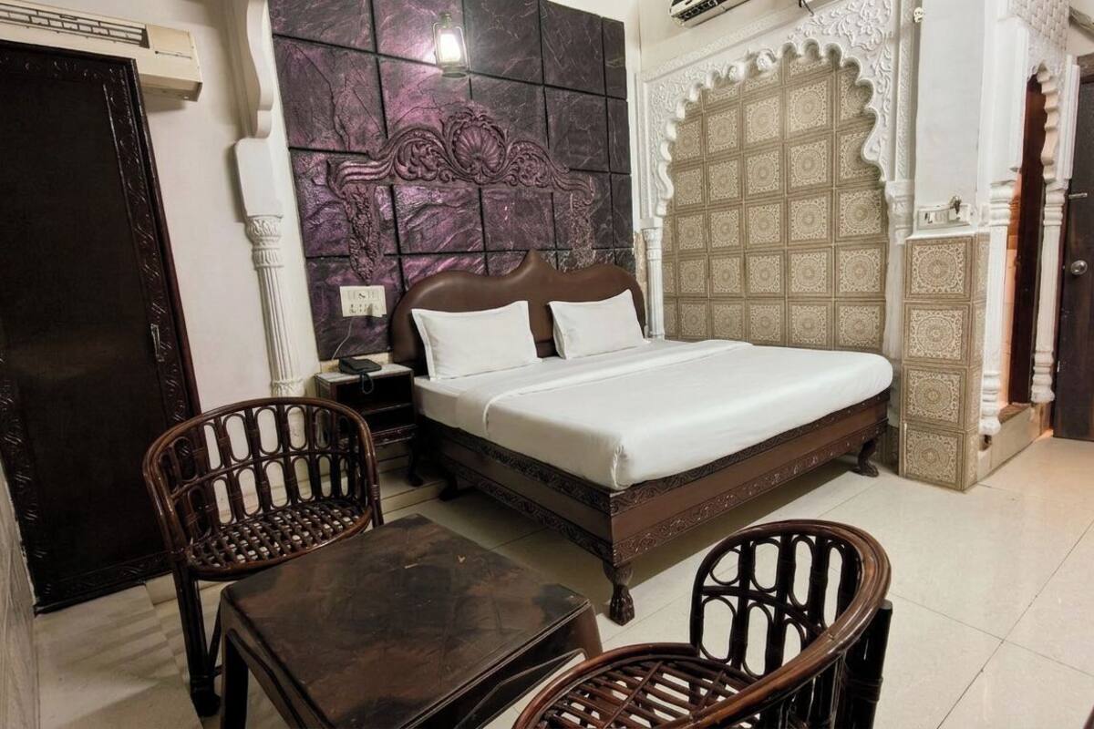 Quarto com cama, duas cadeiras, uma mesa, mesa de cabeceira e decoração na parede.