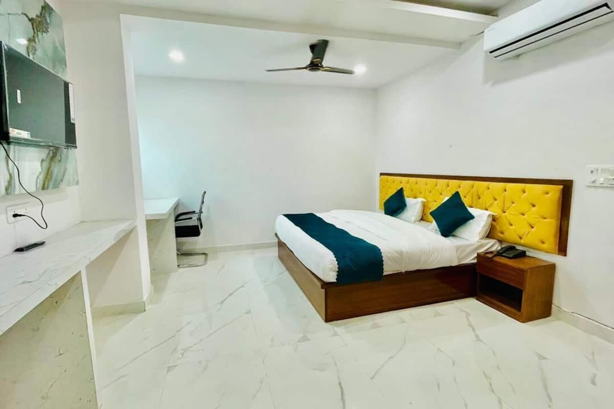 Quarto com cama, mesa de cabeceira, televisão e ventoinha no teto.