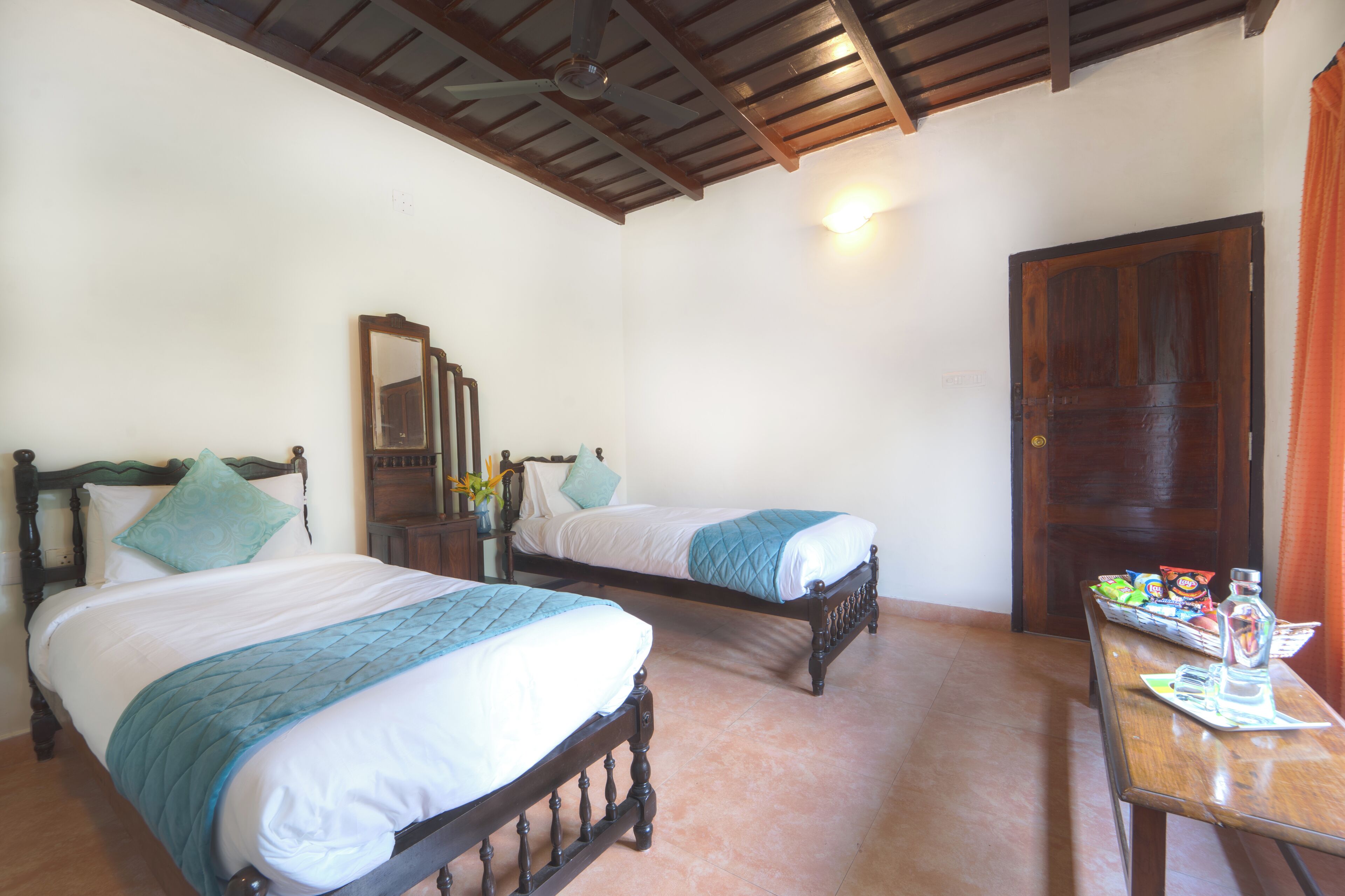 Quarto com duas camas de madeira, uma mesa de madeira com petiscos, um espelho e uma porta.