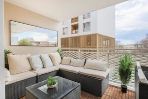 Uma varanda com móveis de vime, um vaso de plantas e vista para um edifício.