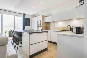 Cozinha moderna com armários brancos, uma ilha central e um espaço de bar com banquetas.