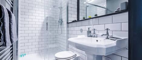Uma casa de banho moderna com chuveiro envidraçado, azulejos brancos, lavatório branco e sanita.