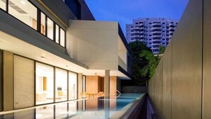 Um edifício moderno com piscina, paredes de vidro e vista para um arranha-céu ao fundo.