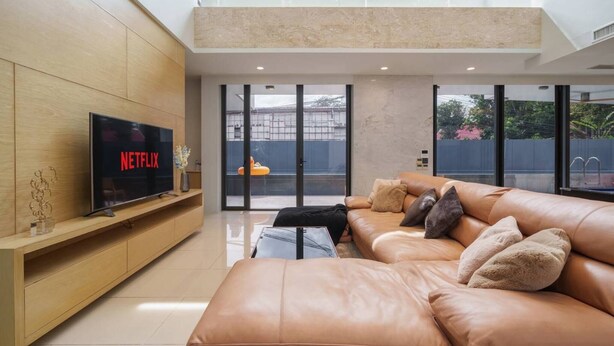 Uma sala de estar moderna com um sofá de couro, uma televisão de tela plana e uma janela grande com vista para o exterior.