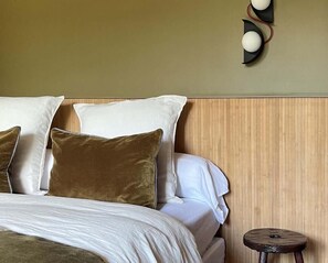 Cama com travesseiros brancos e castanhos, cabeceira de madeira e um banquinho de madeira.