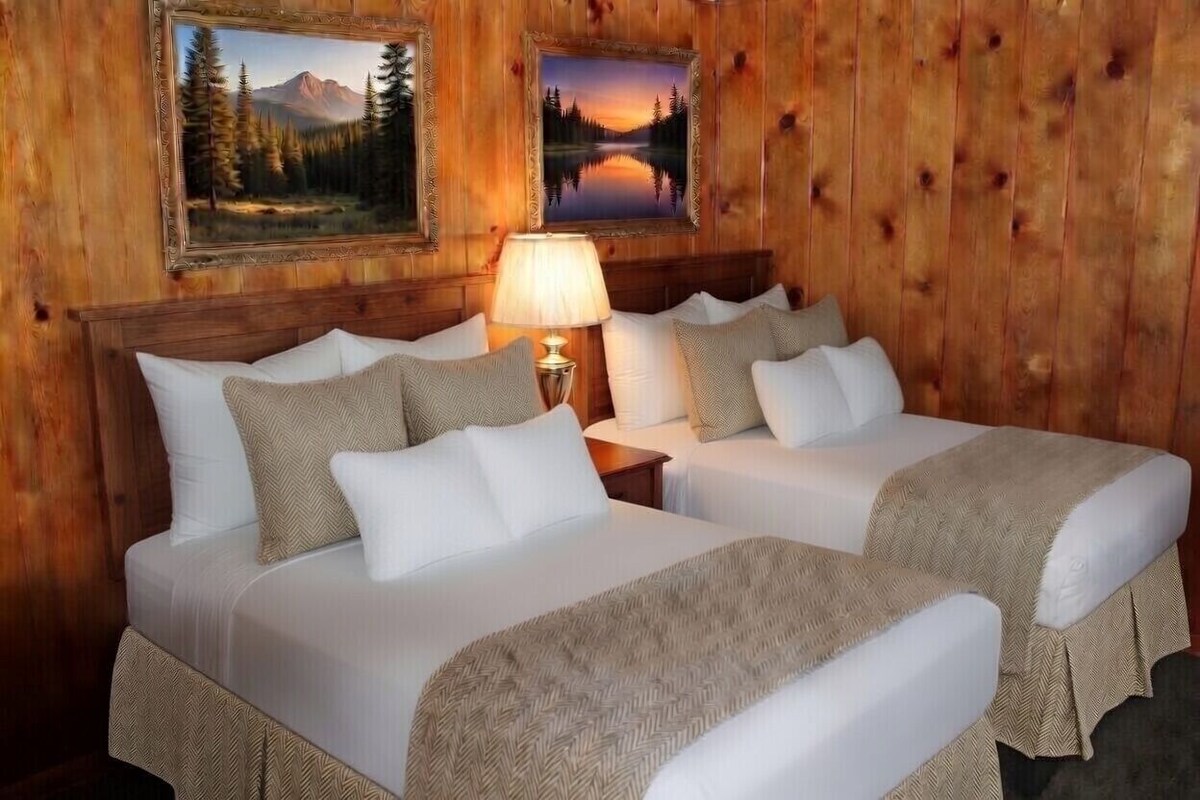 Quarto com duas camas, mesa de cabeceira e abajur.