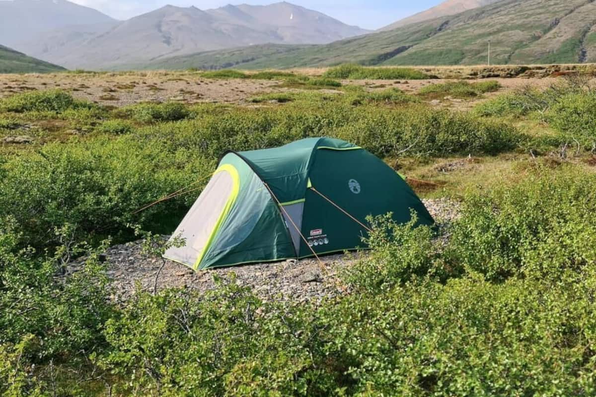 Uma tenda verde montada em uma paisagem natural, com montanhas ao fundo.
