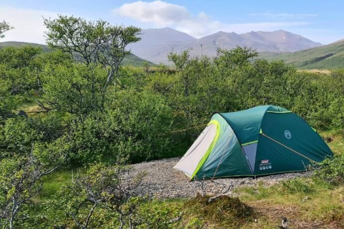 Uma tenda verde montada em uma paisagem natural com montanhas ao fundo.