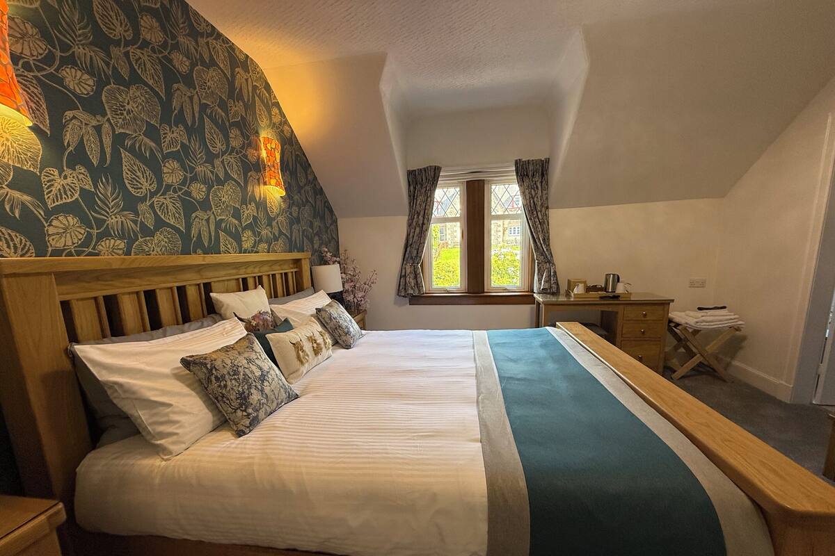 Quarto com cama de madeira, mesa de cabeceira, escrivaninha e janela com cortinas.