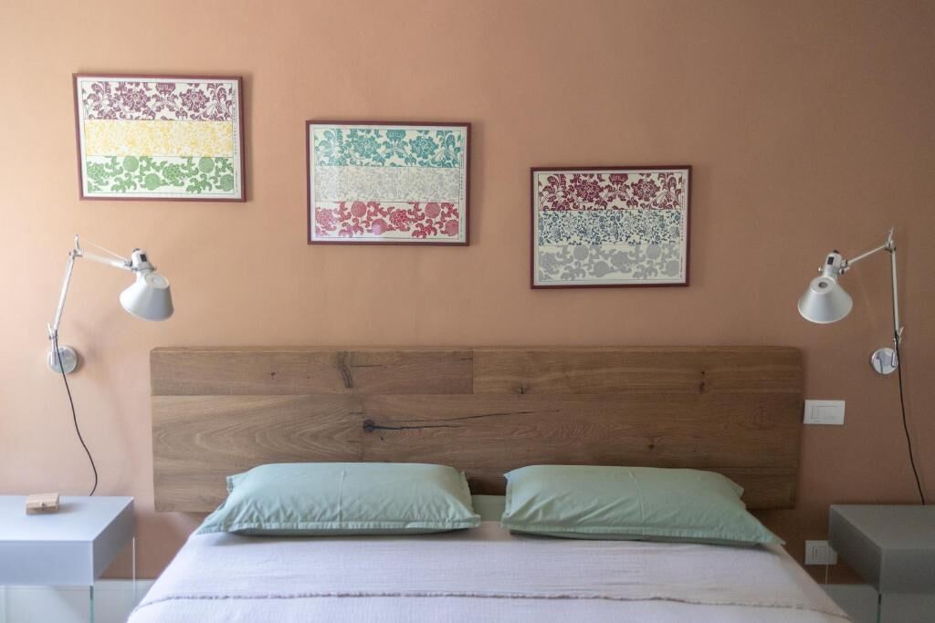 Quarto com cabeceira de madeira, duas mesas de cabeceira, cama com travesseiros verdes e três obras de arte emolduradas na parede.