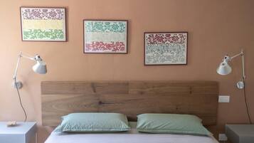 Quarto com cabeceira de madeira, duas mesas de cabeceira, cama com travesseiros verdes e três obras de arte emolduradas na parede.