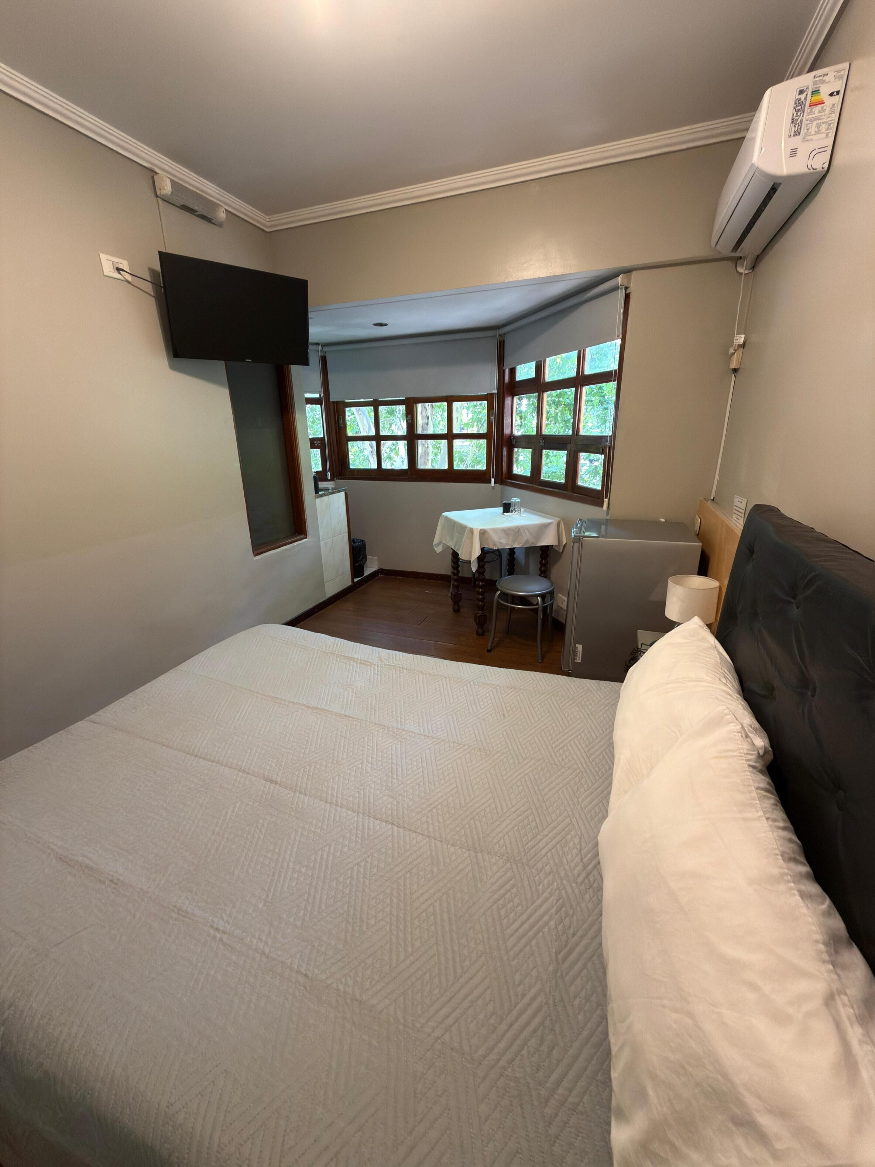 Quarto com cama, escrivaninha, cadeira, janela e ar condicionado.