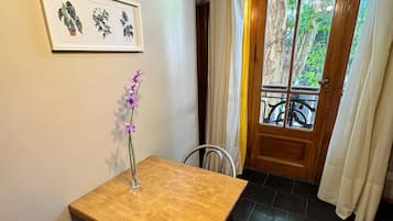 Uma sala de jantar com uma mesa de madeira, cadeiras de metal, um vaso com flores e gravuras botânicas emolduradas na parede.