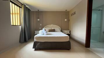 Quarto moderno com cama grande, mesas de cabeceira, ventilador de teto e vista para um espaço com chuveiro.