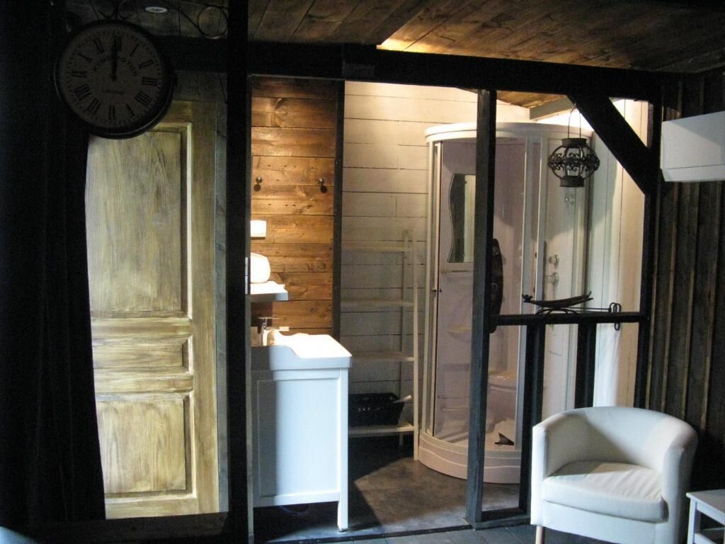 Interior em madeira com uma pia branca, uma cadeira branca e área de chuveiro com divisória de vidro.