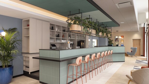 Uma área de bar moderna com um balcão comprido, vários bancos e prateleiras com copos e garrafas.