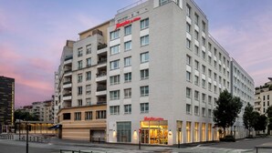 Um hotel com vários andares, fachada plana, janelas amplas e entrada visível.