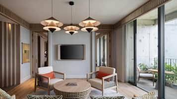 Uma sala de estar moderna com um sofá, duas poltronas, uma mesa de centro e iluminação pendente. Uma televisão de tela plana está fixada na parede.