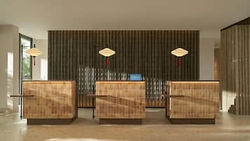 Uma área de recepção com três balcões de madeira, uma parede com padrão de bambu vertical e duas luminárias pendentes.