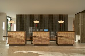 Uma área de recepção com três balcões de madeira, uma parede com padrão de bambu vertical e duas luminárias pendentes.