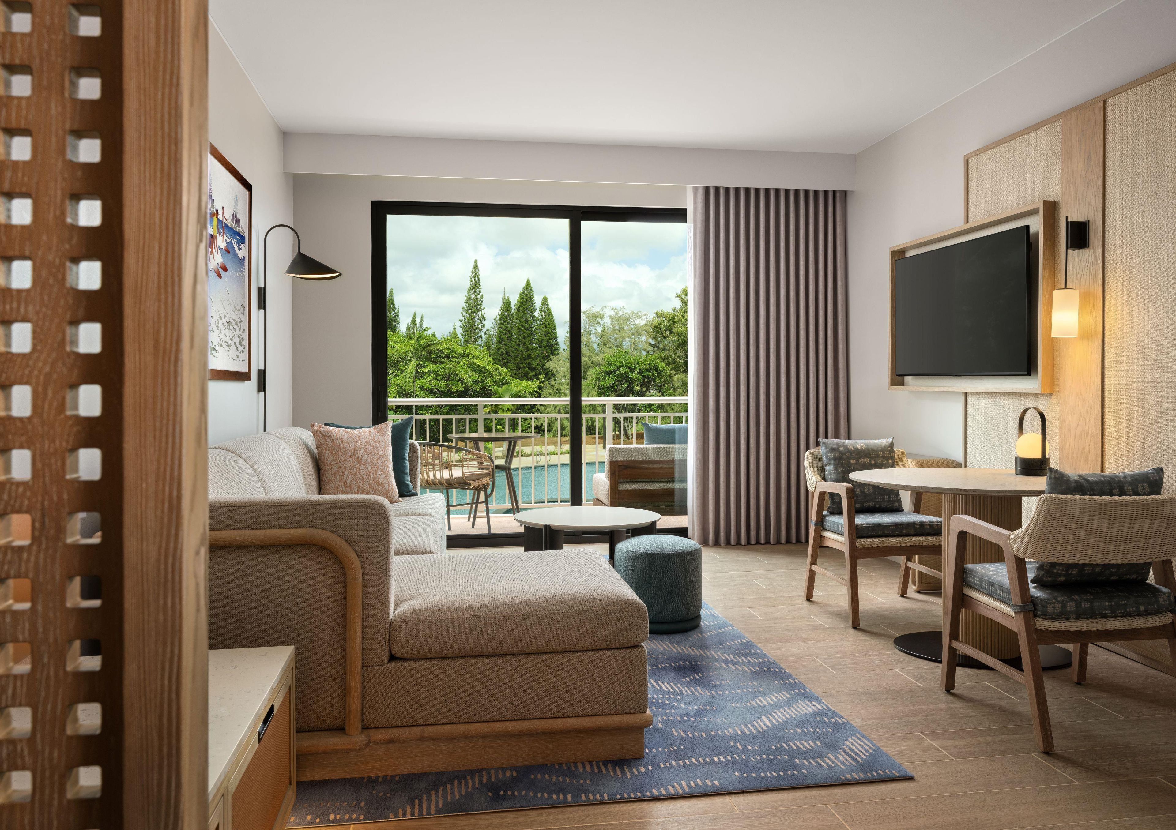 Uma sala de estar moderna com sofá, cadeiras, mesa de centro, televisão e varanda com vista para a piscina.