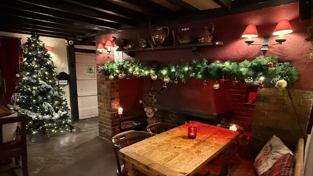 Um quarto acolhedor com uma mesa de madeira, cadeiras, um pinheiro de Natal e uma lareira decorada com guirlandas.