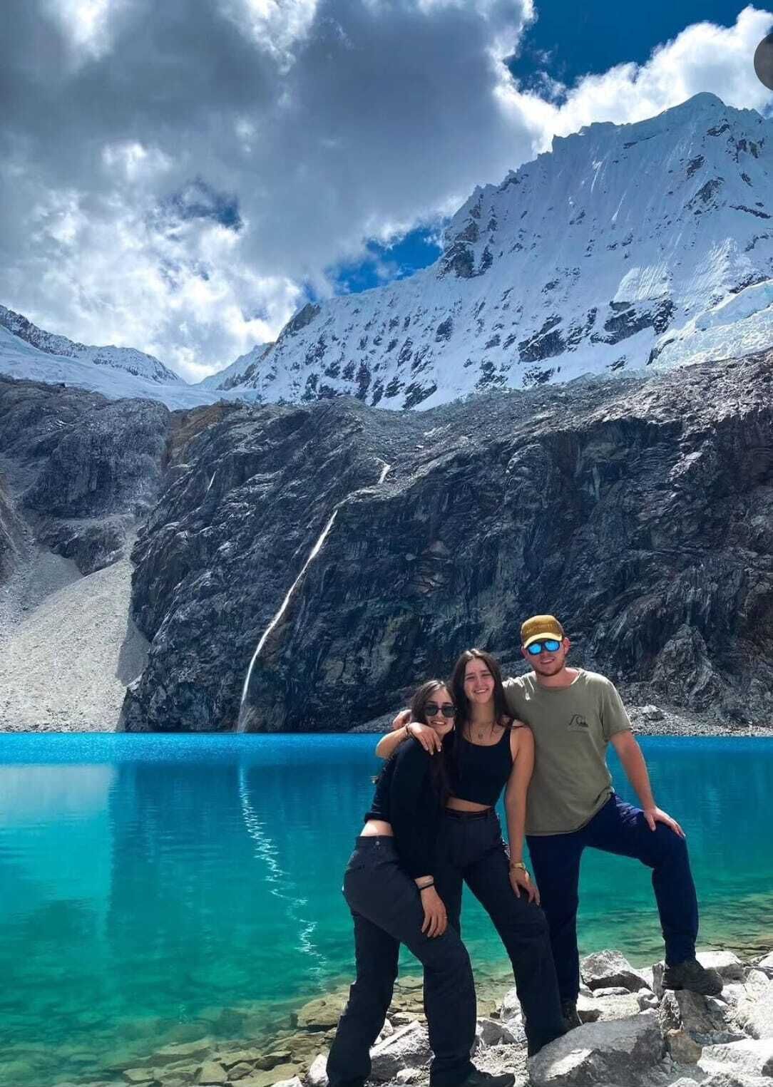 Um grupo de pessoas perto de um lago azul e límpido, com montanhas ao fundo.