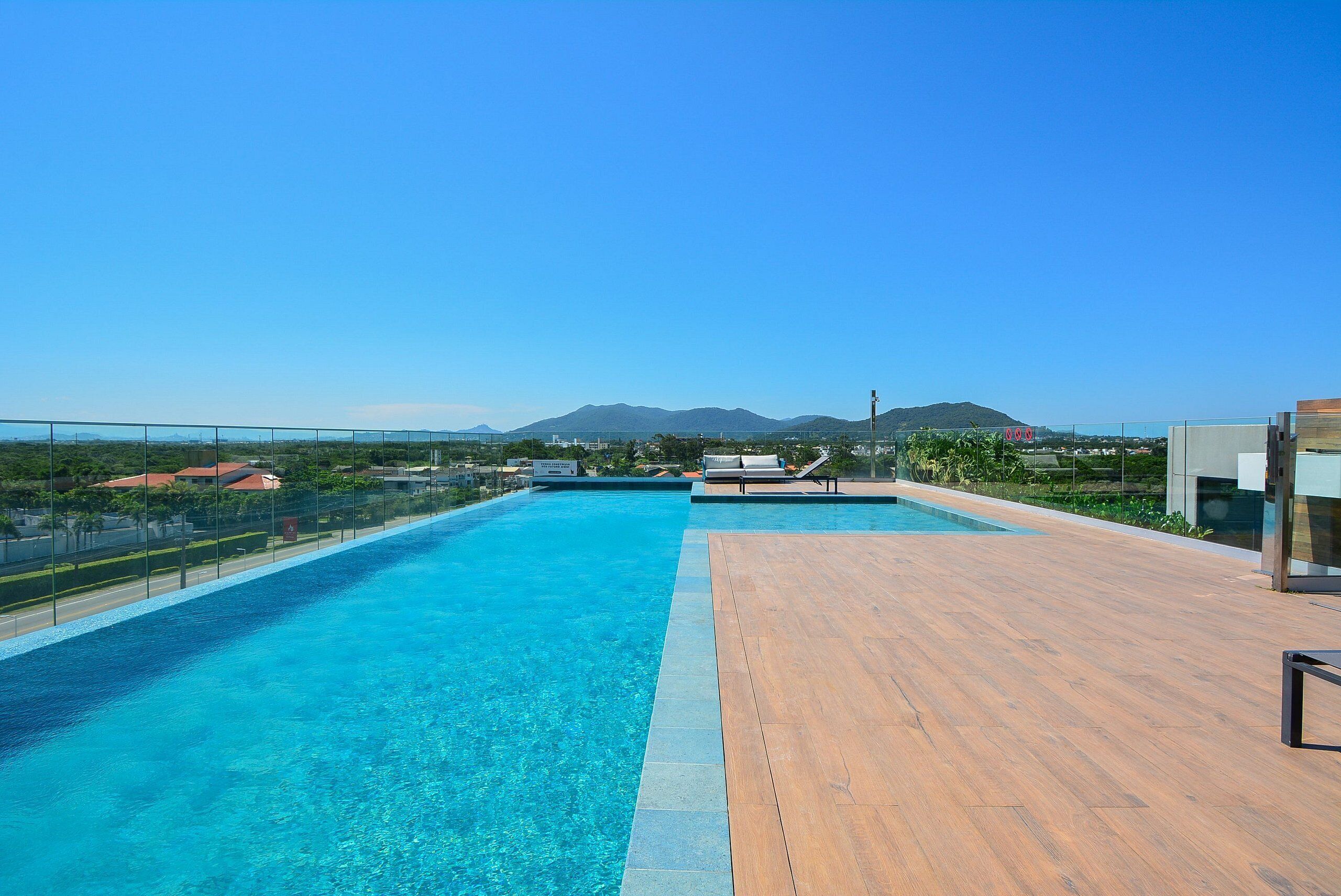 Piscina no terraço com água azul cristalina, deck de madeira e vista para montanhas distantes.