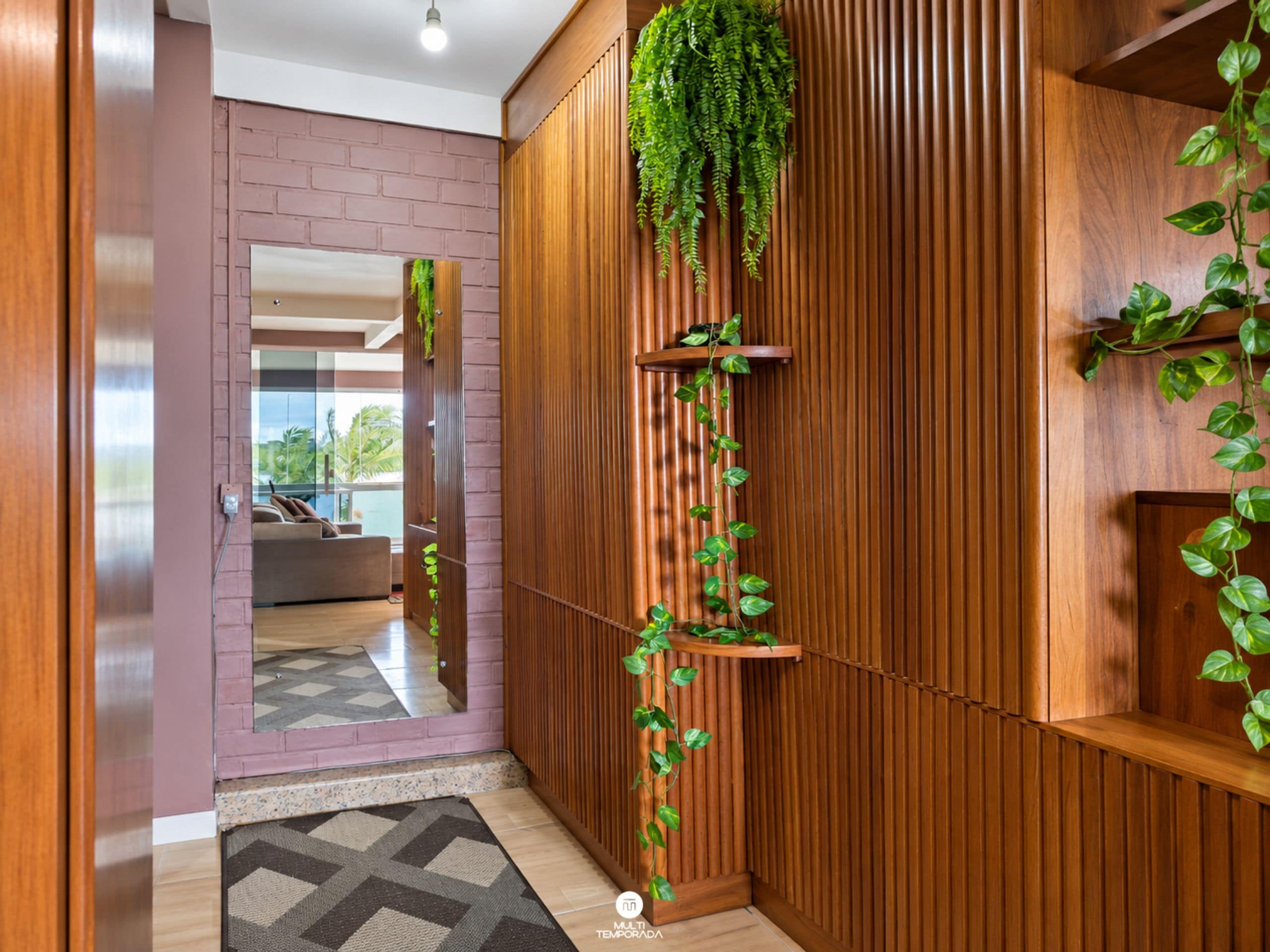 Um corredor com parede de painel de madeira, espelho e planta pendente.