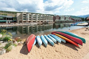 Hotel na orla marítima com vários edifícios, um cais com barcos e uma área de praia arenosa.