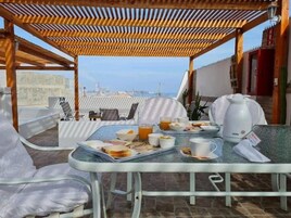 Uma área de refeições coberta ao ar livre, com mesa posta para o café da manhã, cadeiras e vista para o mar.