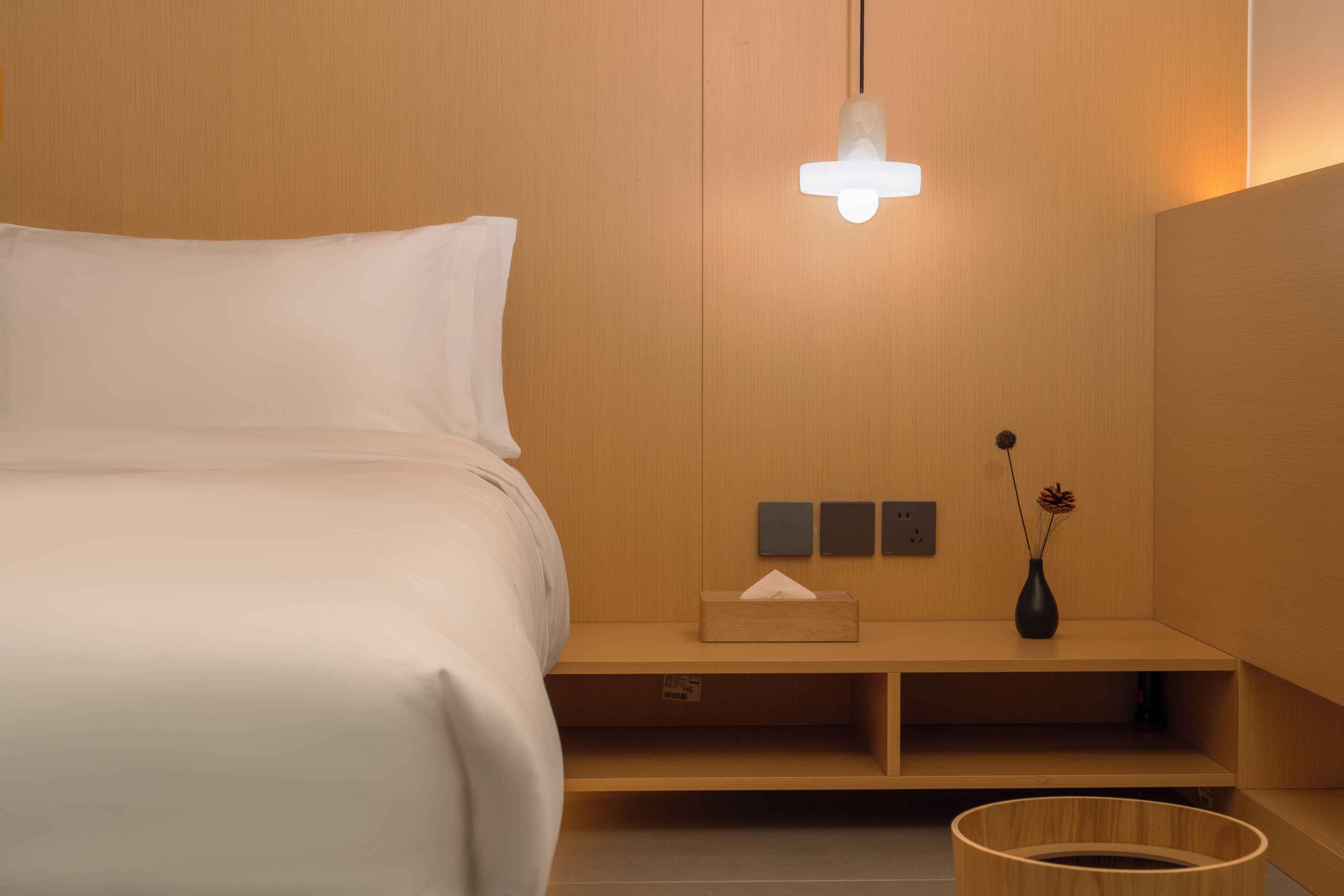 Quarto de hotel com cama, mesa de cabeceira com vaso e luminária na parede.