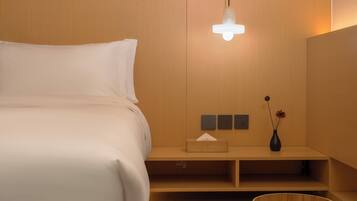Quarto de hotel com cama, mesa de cabeceira com vaso e luminária na parede.
