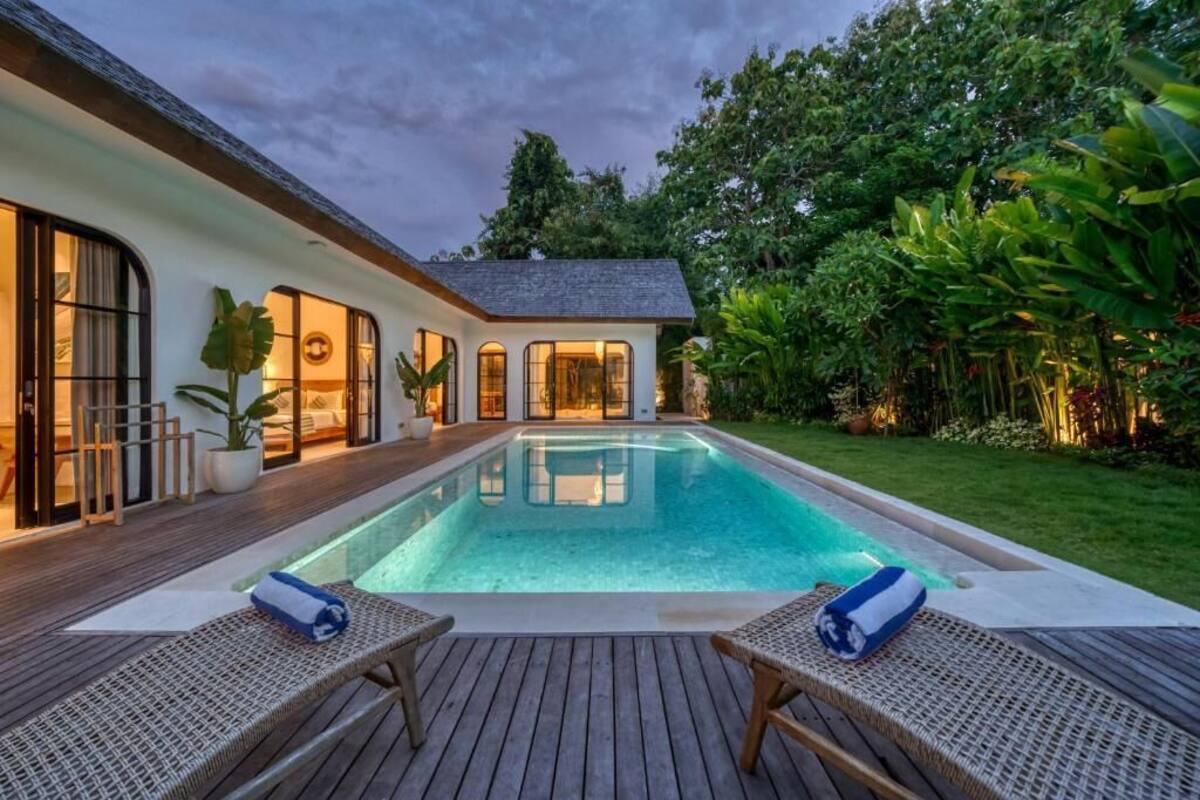 Uma piscina com espreguiçadeiras, um deck de madeira e uma casa com grandes janelas.