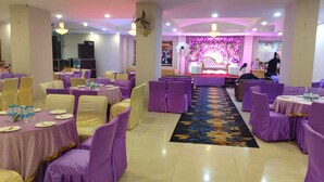 Salão de banquetes com mesas redondas, cadeiras roxas e um tapete floral.