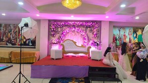 Um palco com um sofá branco e um tapete vermelho, rodeado por decorações florais e um candelabro.