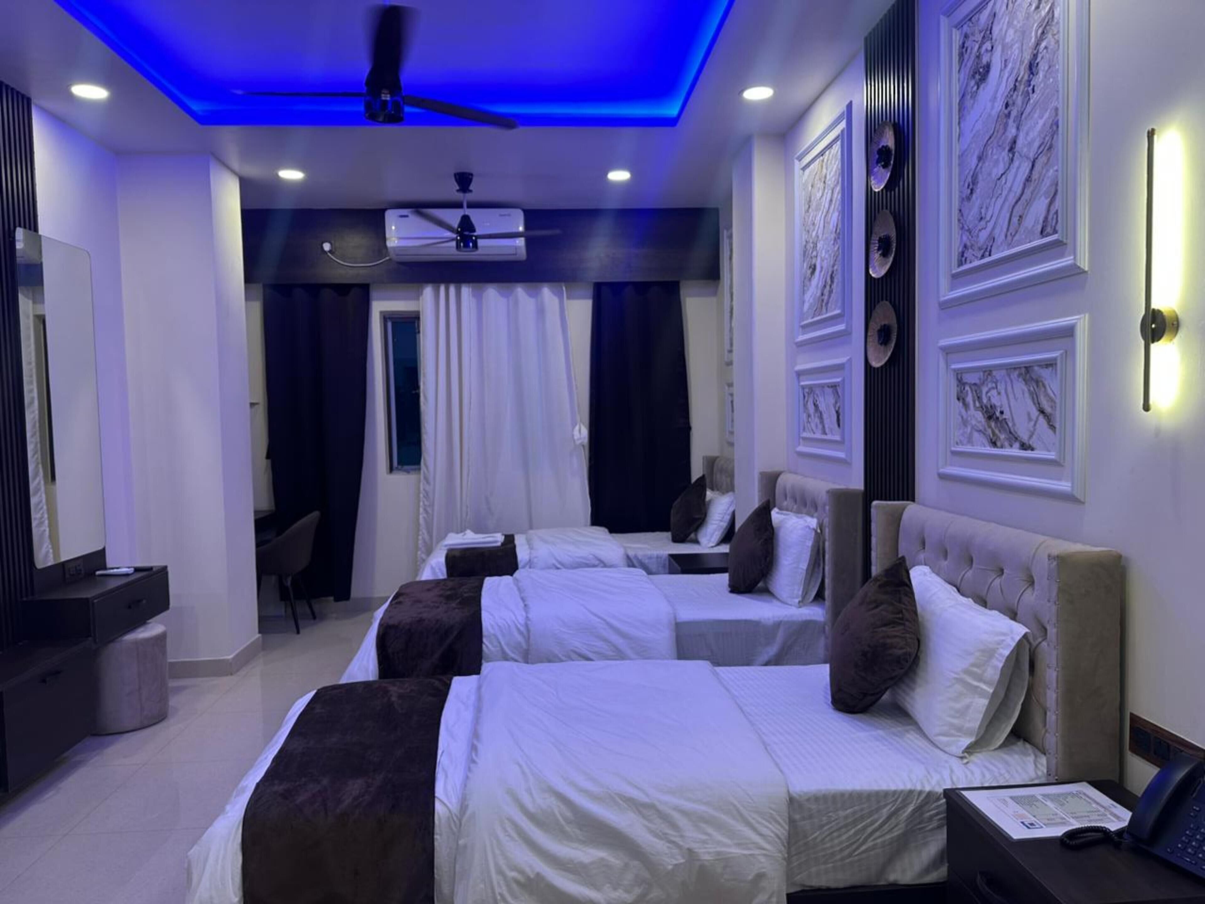 Quarto de hotel com duas camas, um ventilador de teto, um projetor e obras de arte nas paredes.