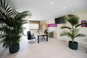 Um espaço de escritório moderno com uma mesa de reuniões, cadeiras, uma TV na parede e plantas em vasos.