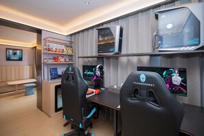 Uma sala de jogos com dois monitores, cadeiras gamer e prateleiras com lanches.