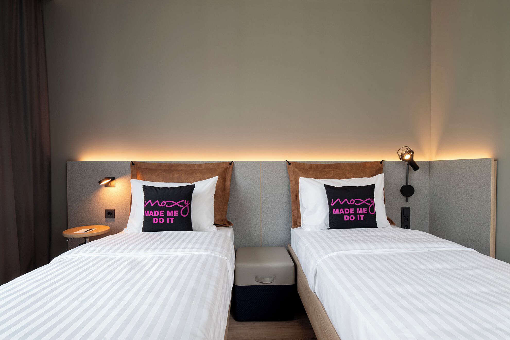 Quarto de hotel com duas camas, cada uma com um travesseiro com a inscrição 'moosy made me do it'.