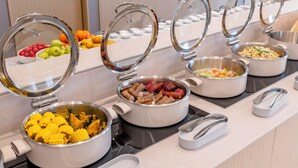 Disposição de buffet com diversos alimentos em tigelas e panelas, micro-ondas e máquina de café.