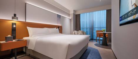Quarto de hotel moderno com uma cama grande, uma mesa de cabeceira com abajur, TV na parede e varanda com vista.