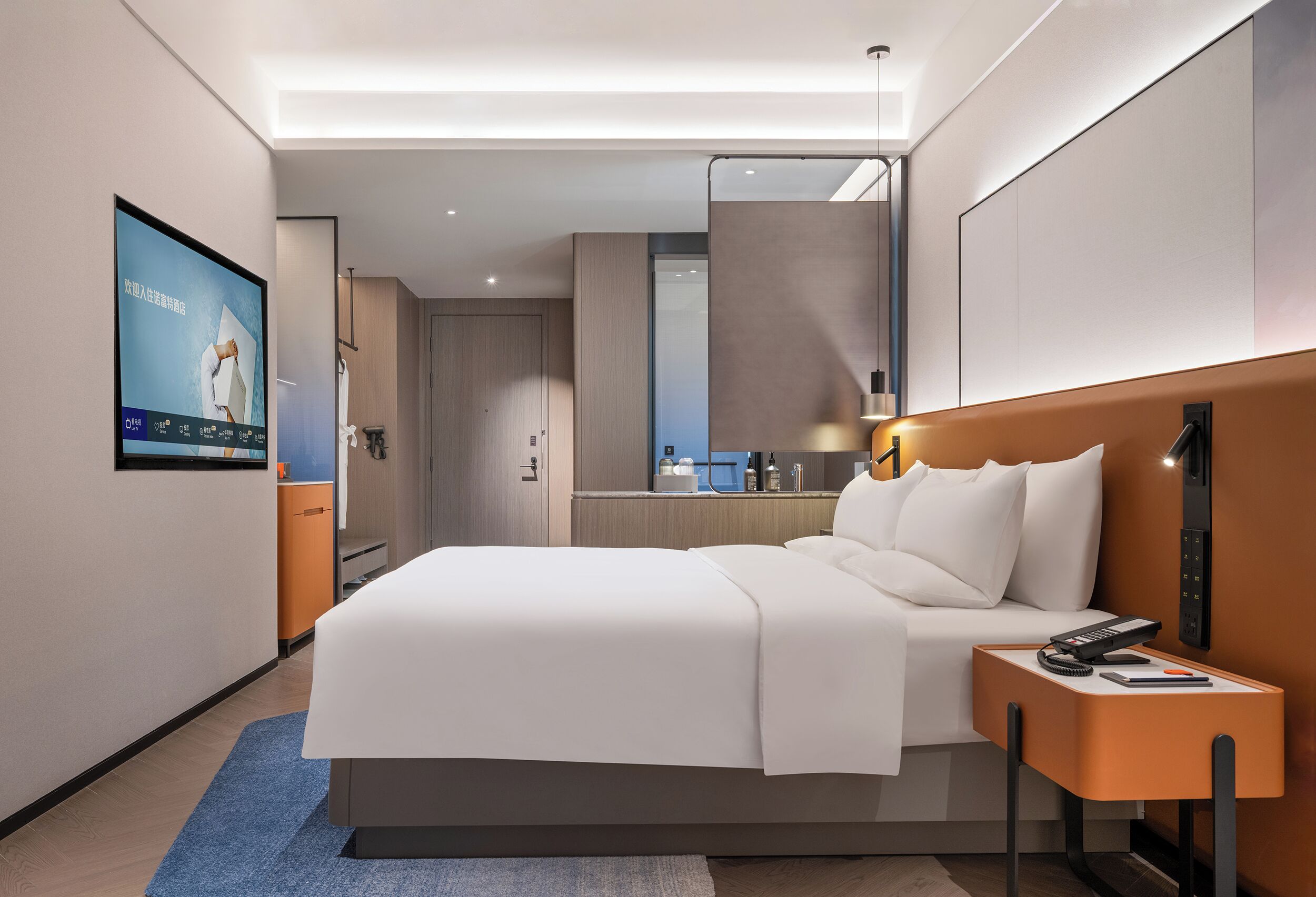Quarto de hotel moderno com uma cama grande, uma mesa de cabeceira com telefone e controle remoto, um espelho e uma TV na parede.