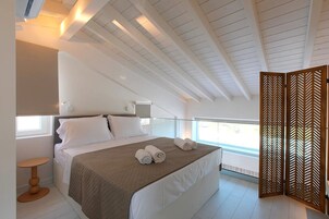 Quarto com cama, mesas de cabeceira, janela e vista para o exterior.