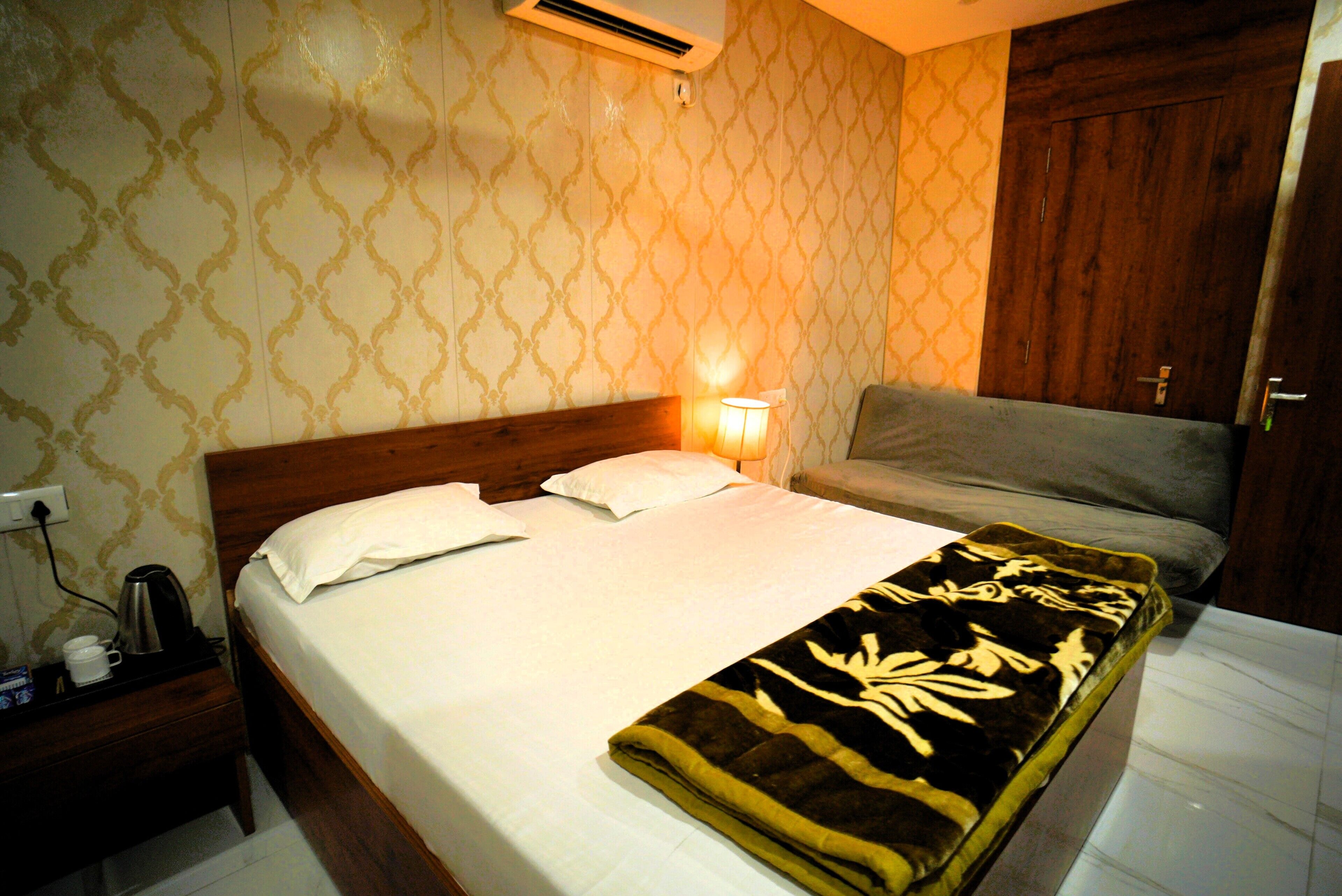Quarto de hotel com cama, mesa de cabeceira, luminária e guarda-roupa.