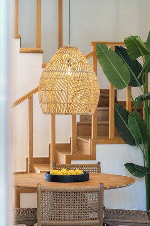 Uma sala de jantar com uma mesa redonda de madeira, cadeiras de vime e um lustre de rattan suspenso.